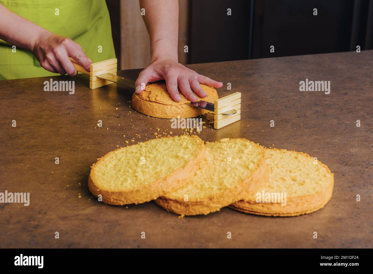 Female baker slicing traditional sponge cake into layers using special ...