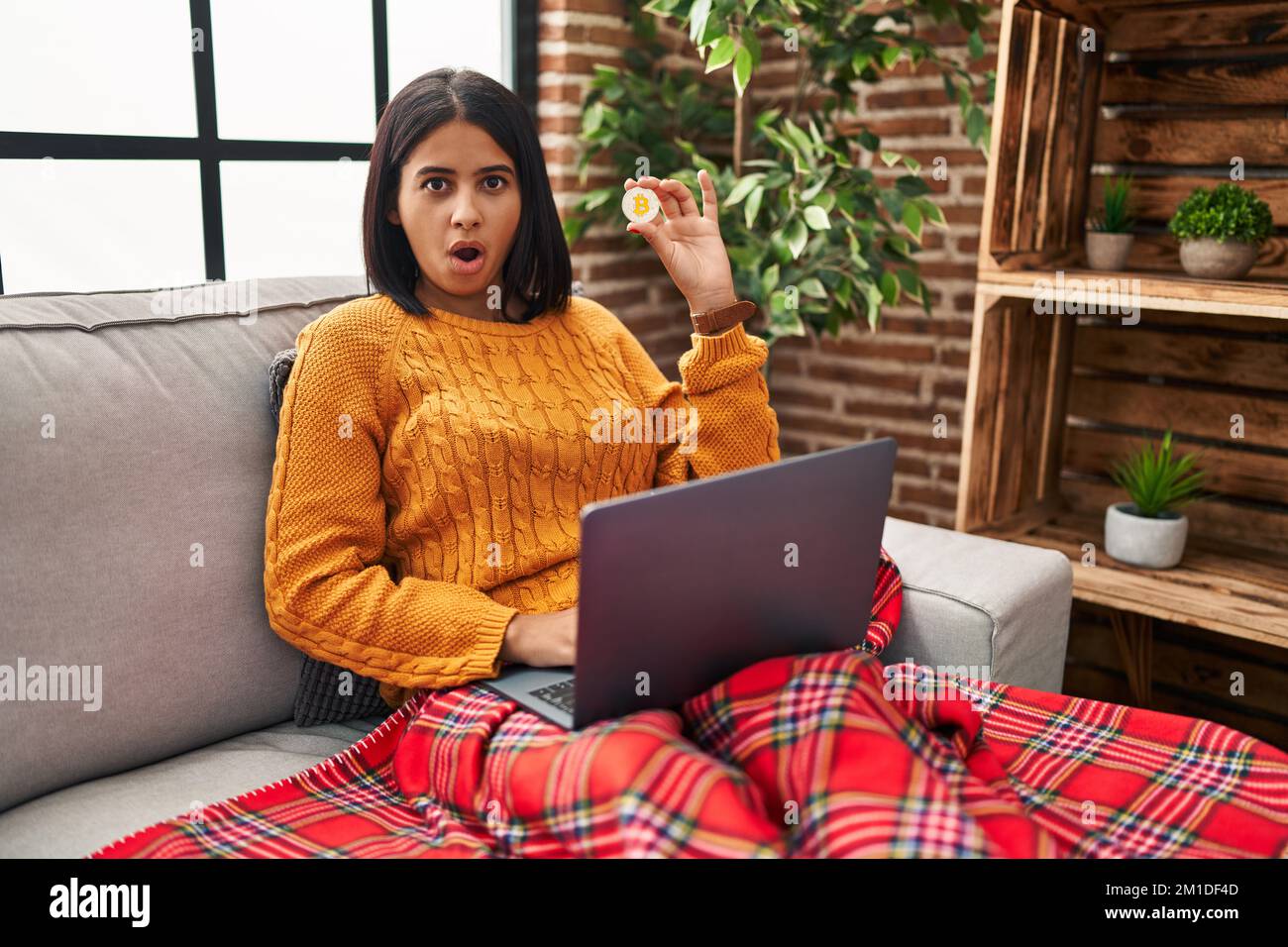 Young hispanic woman using laptop holding virtual currency bitcoin ...