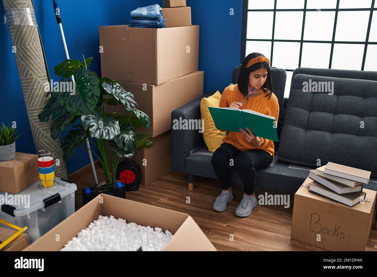 Young latin woman reading book sitting on sofa at new home Stock Photo ...