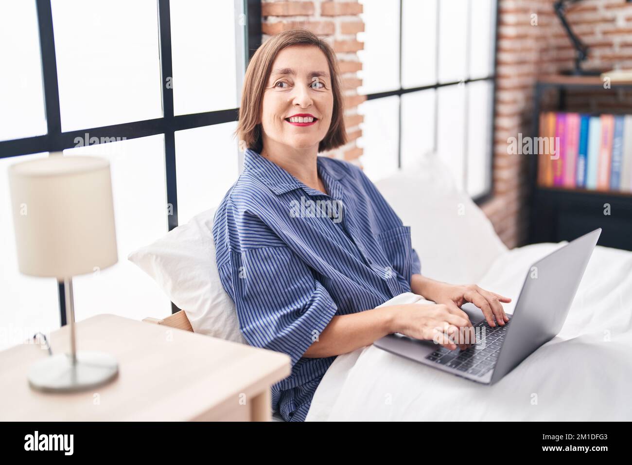 Middle age woman using laptop sitting on bed at bedroom Stock Photo - Alamy