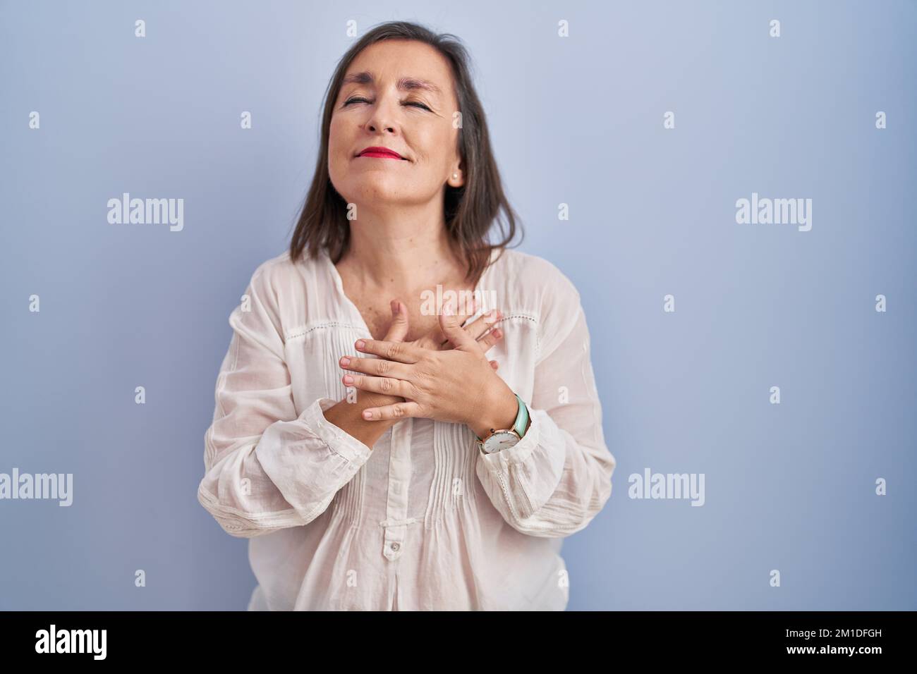 Middle age hispanic woman standing over blue background smiling with ...