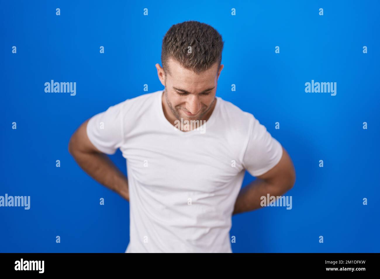 Young caucasian man standing over blue background suffering of backache ...