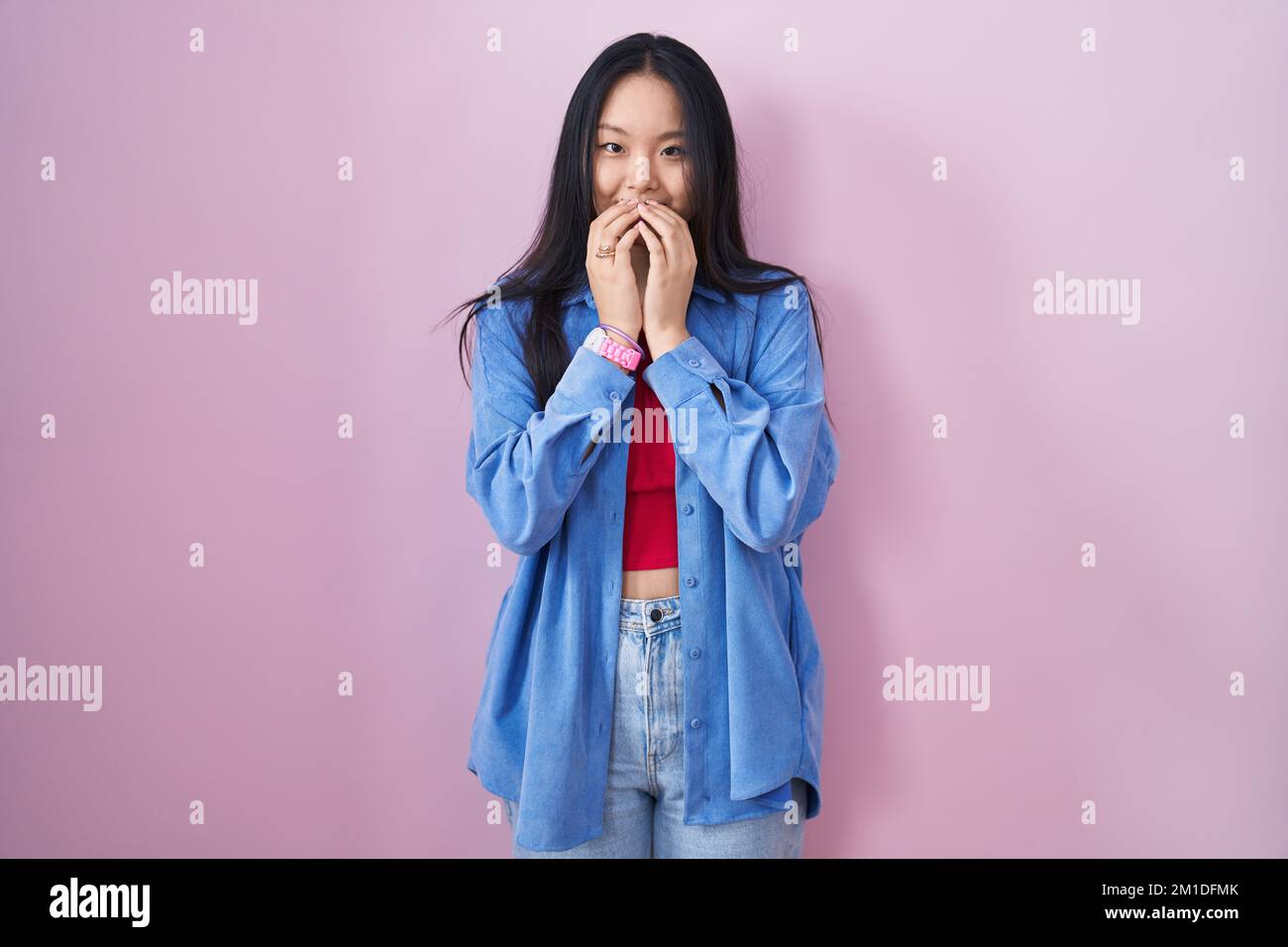 Young asian woman standing over pink background laughing and ...