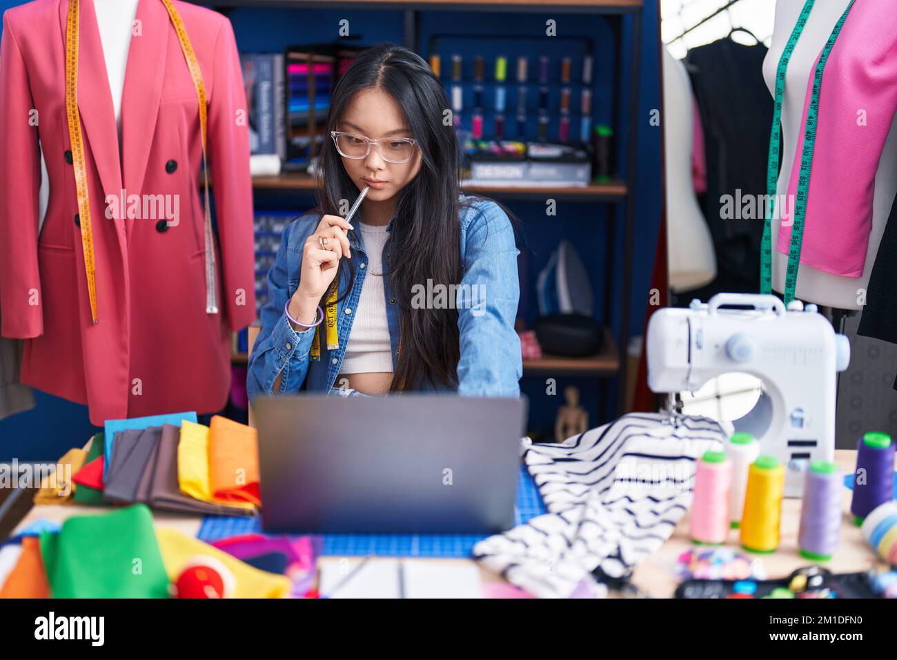 Young chinese woman tailor using laptop with doubt expression at ...