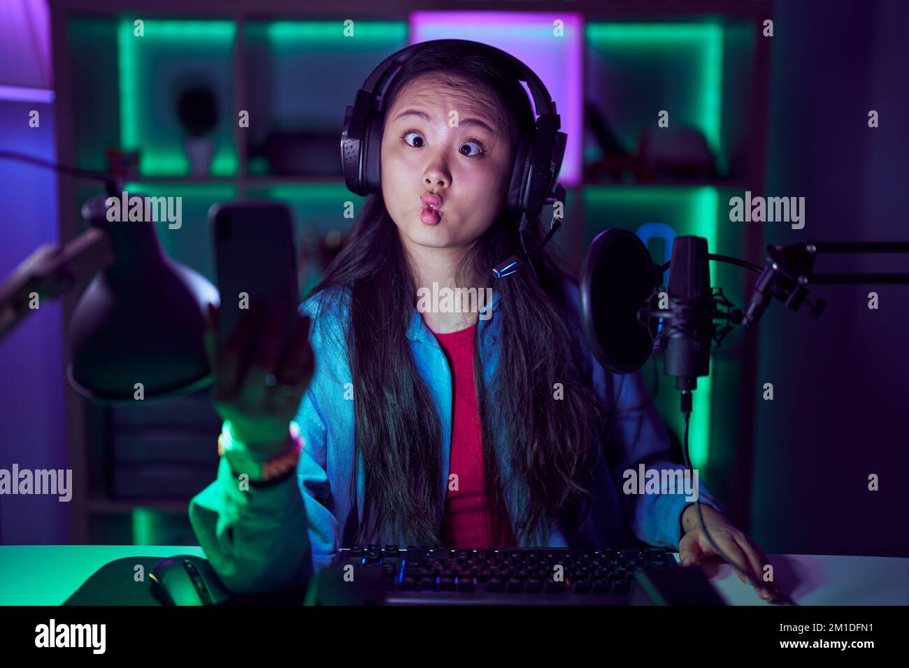 Young asian woman playing video games with smartphone making fish face ...