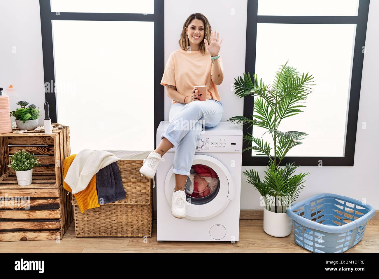 Young hispanic woman drinking coffee waiting for washing machine at ...