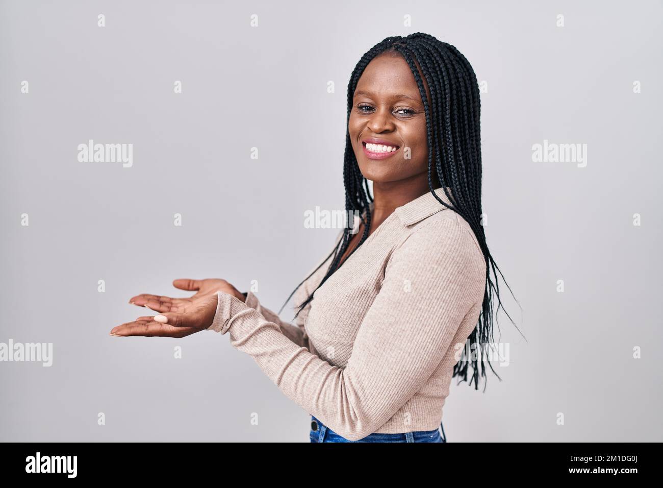 African woman with braids standing over white background pointing aside ...