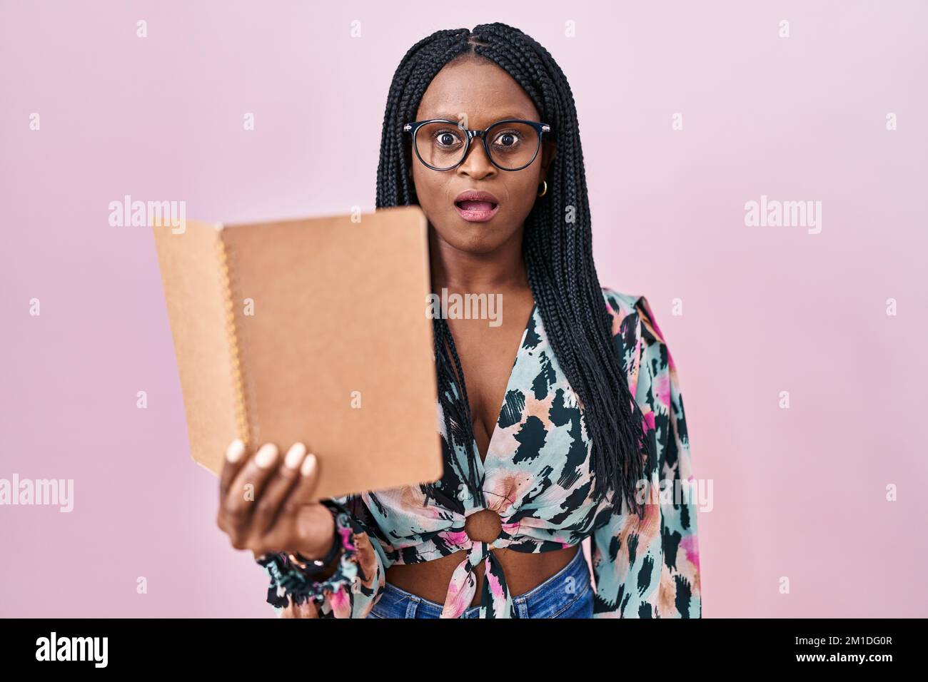 African woman with braids reading a book scared and amazed with open ...