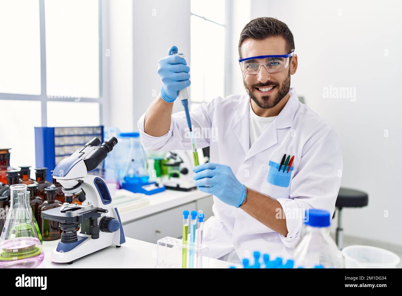 Young hispanic man wearing scientist uniform using pipette and test ...