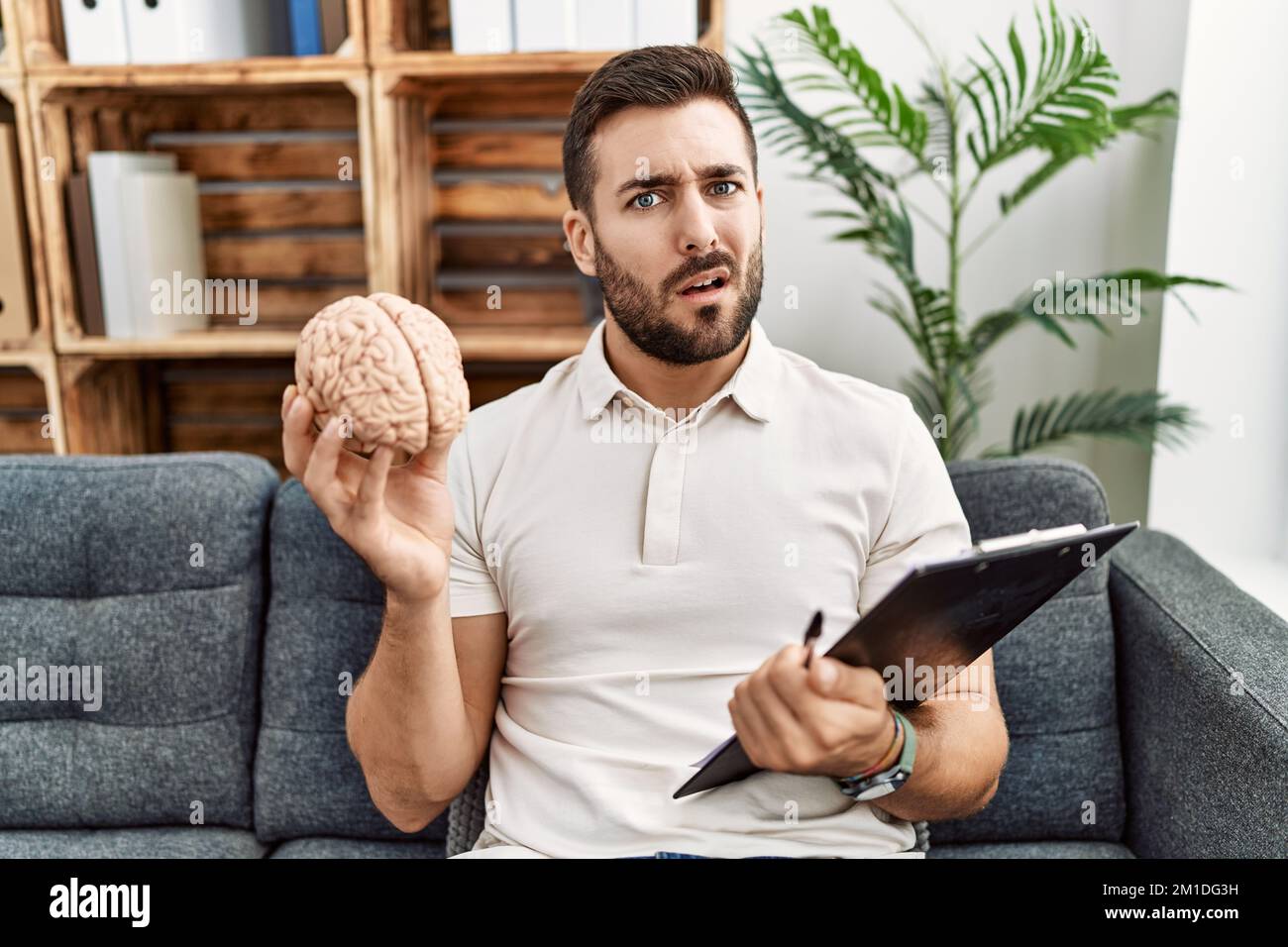 Handsome hispanic man holding brain working at psychology clinic ...
