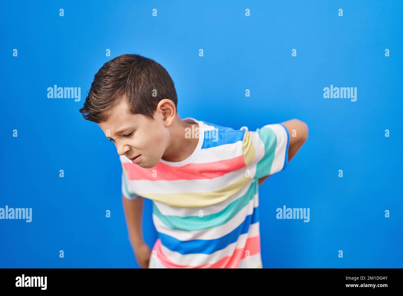 Young caucasian kid standing over blue background suffering of backache ...