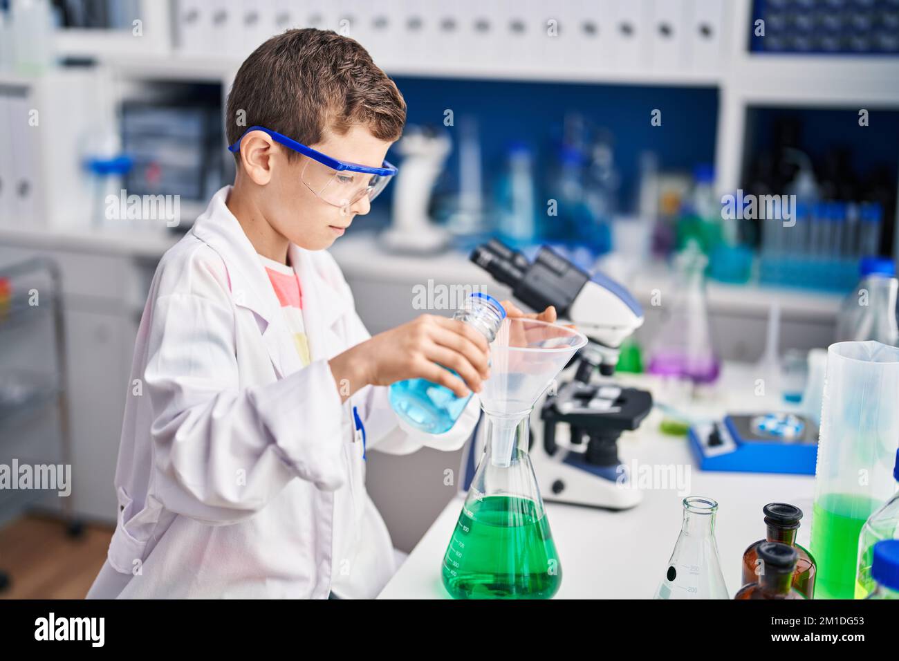 Blond child wearing scientist uniform measuring liquid at laboratory ...