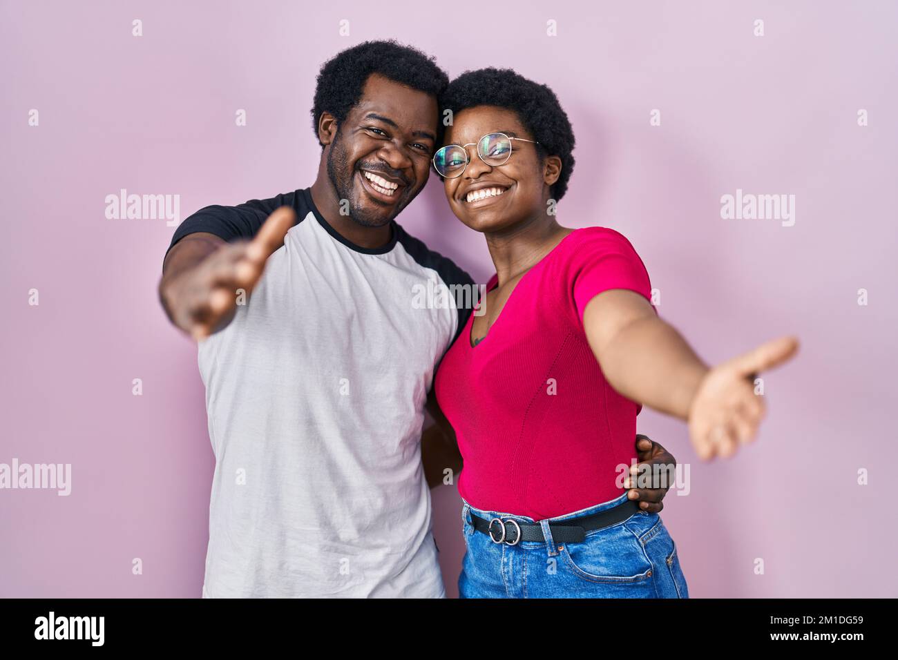 Young african american couple standing over pink background looking at ...