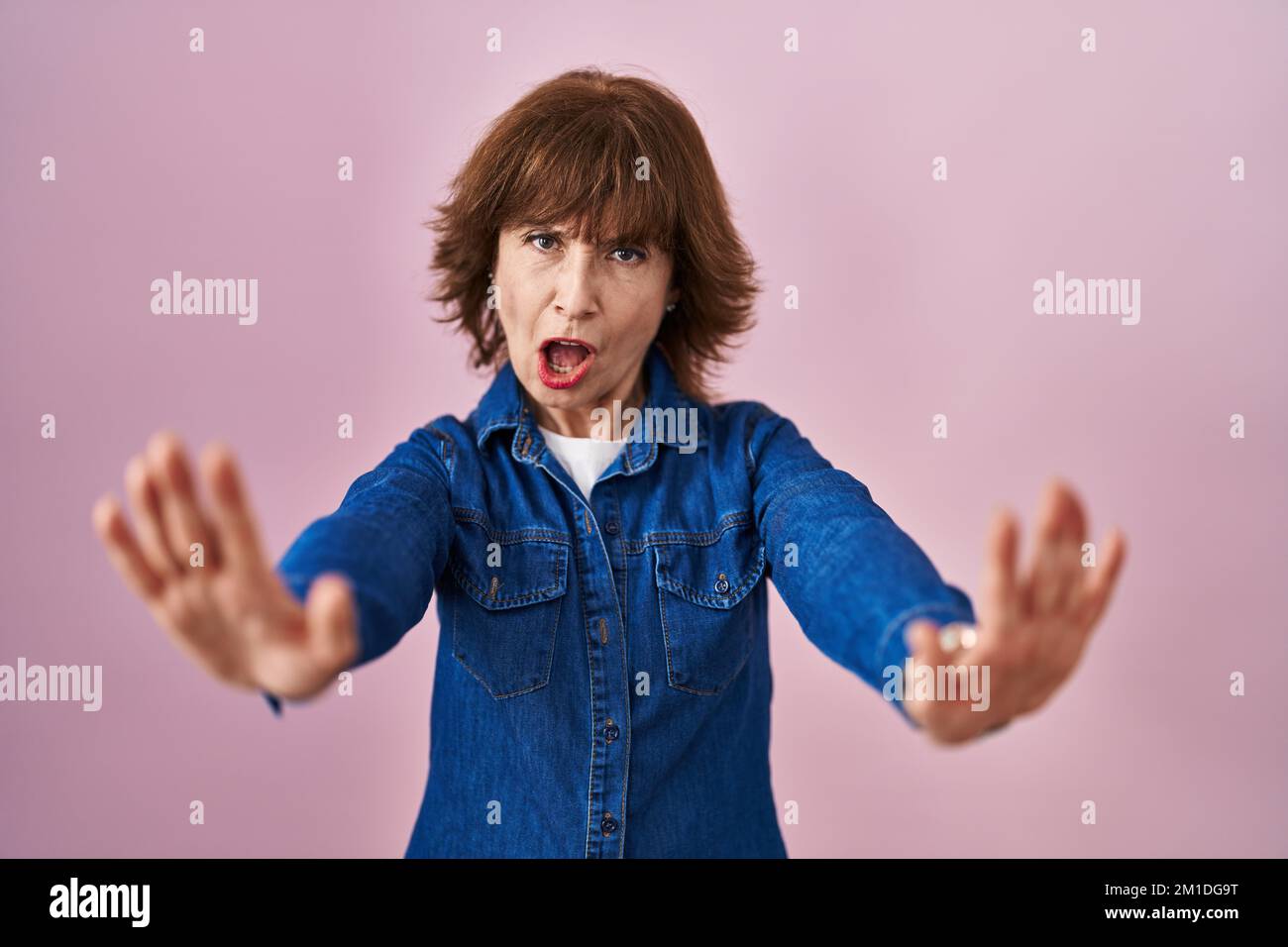 Middle age woman standing over pink background doing stop gesture with ...
