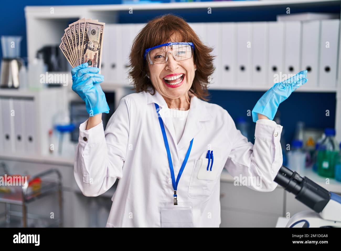 Middle age woman working at scientist laboratory holding money ...
