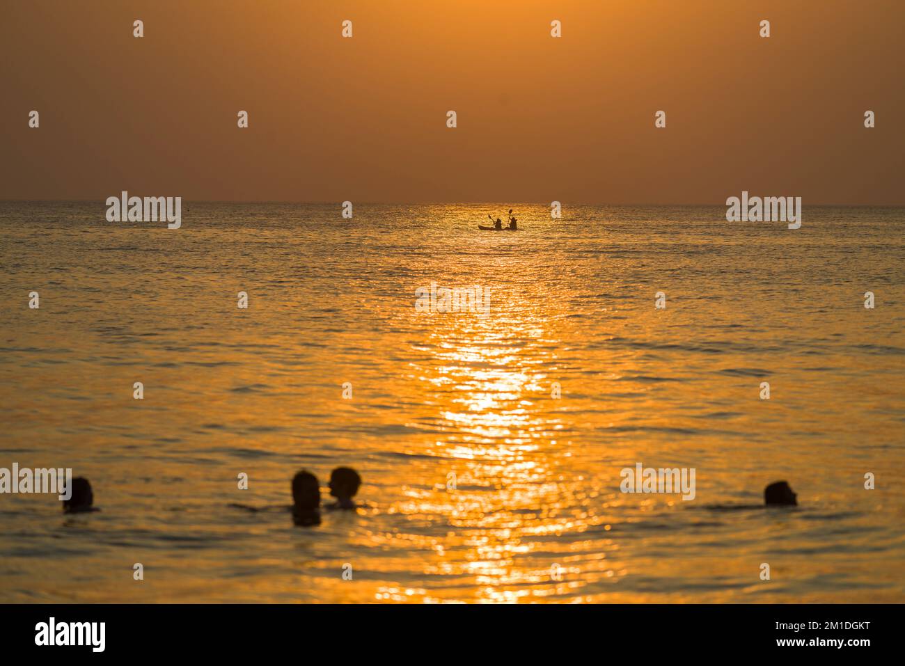 Two people in a kayak are canoeing in the open sea at sunset at Palolem ...
