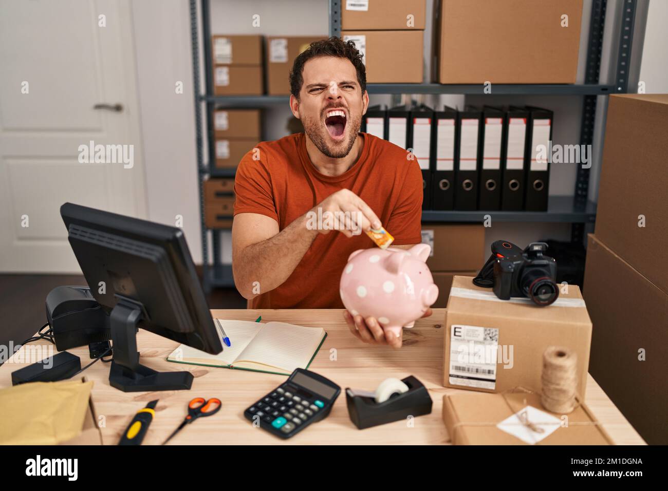 Young hispanic man working at small business ecommerce holding piggy ...