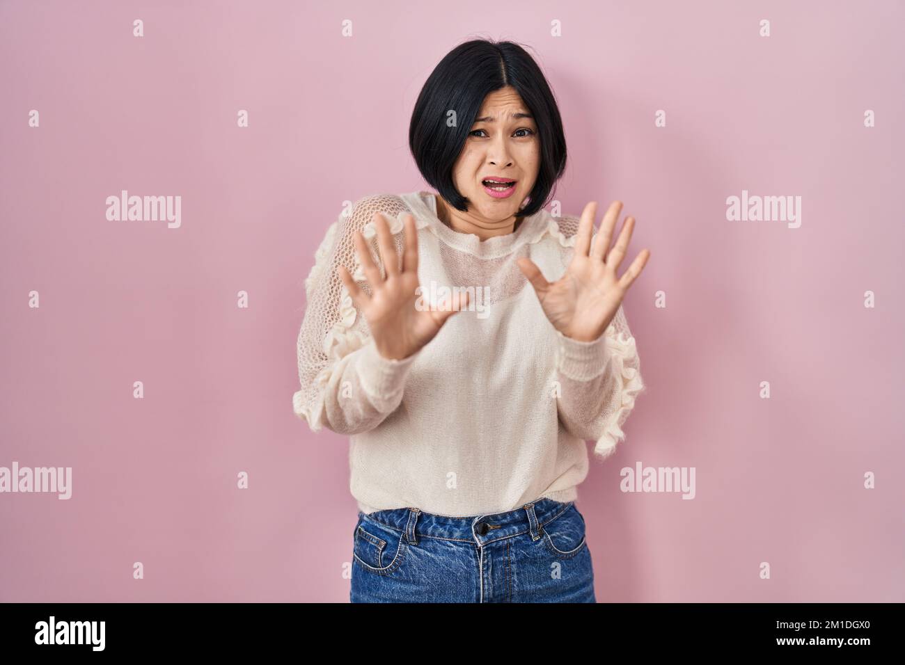 Young asian woman standing over pink background afraid and terrified ...