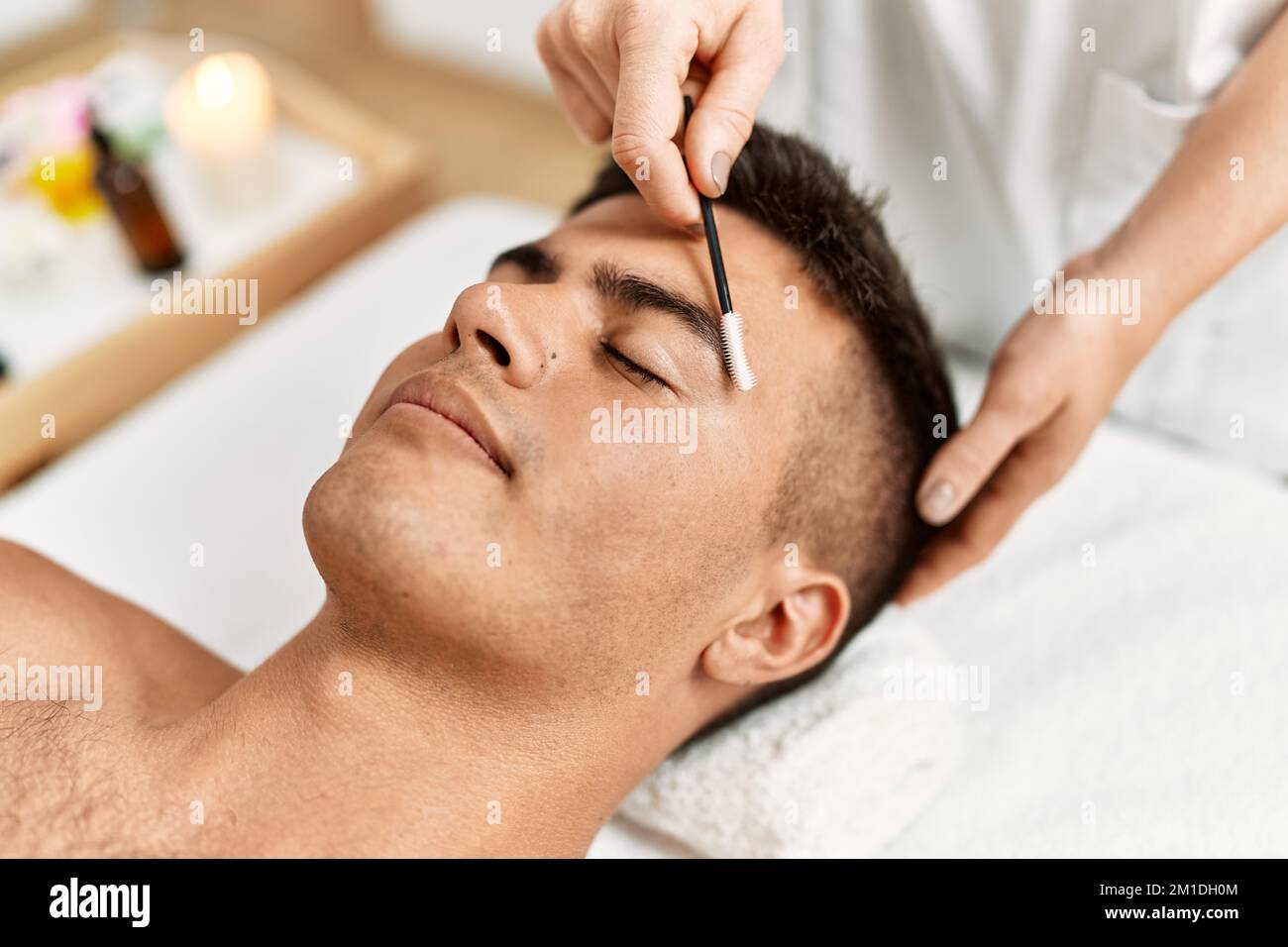 Young hispanic man relaxed having eyebrows treatment at beauty center ...