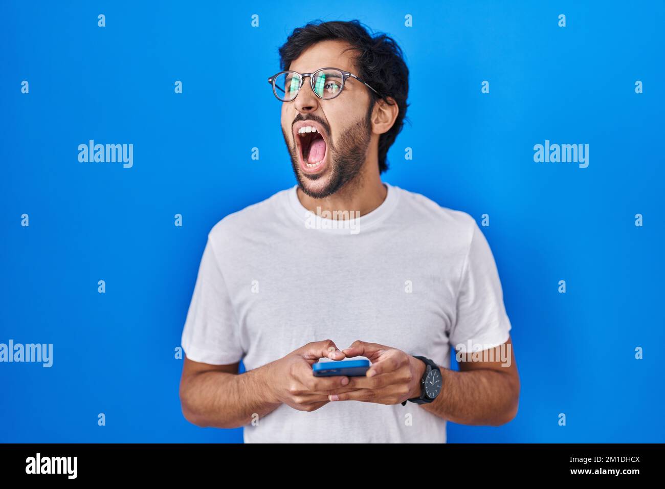 Handsome latin man using smartphone typing message angry and mad ...