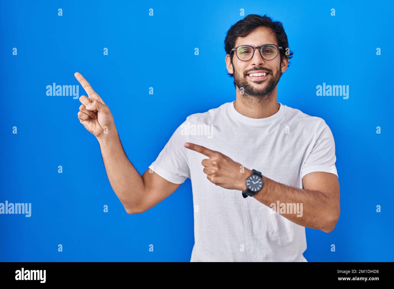 Handsome latin man standing over blue background smiling and looking at ...