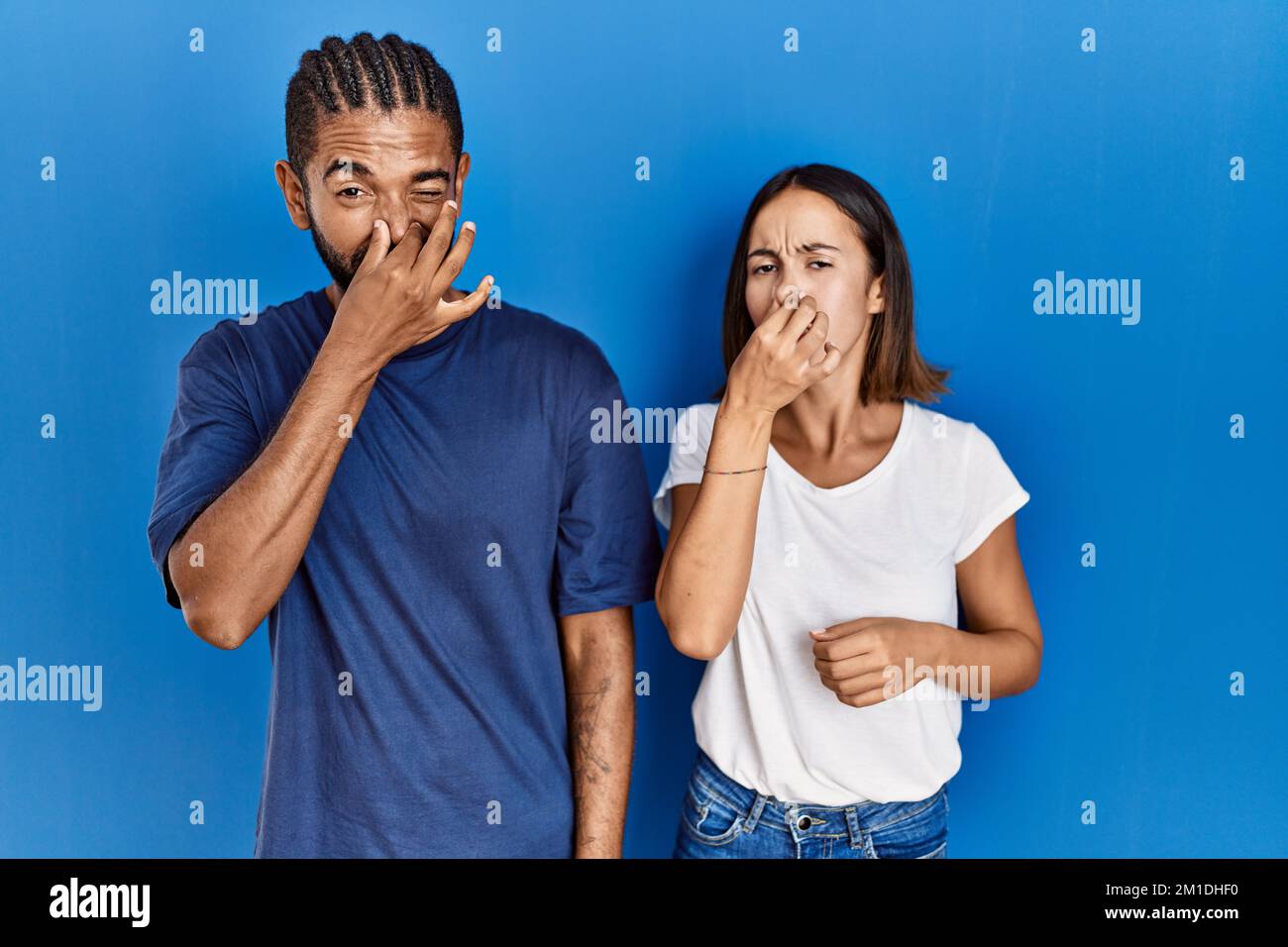 Young hispanic couple standing together smelling something stinky and ...