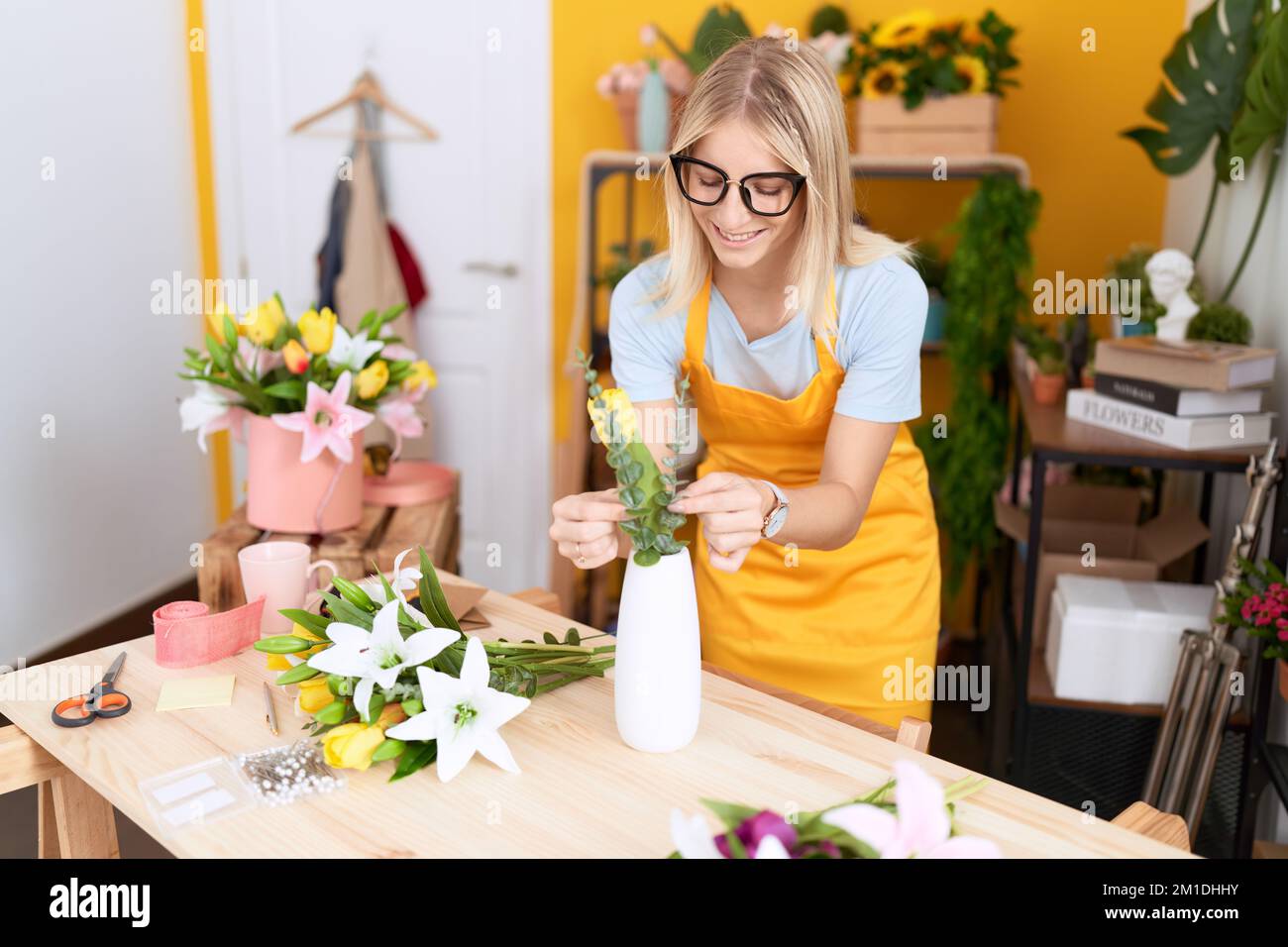 Young blonde woman florist smiling confident putting flowers on jar at ...