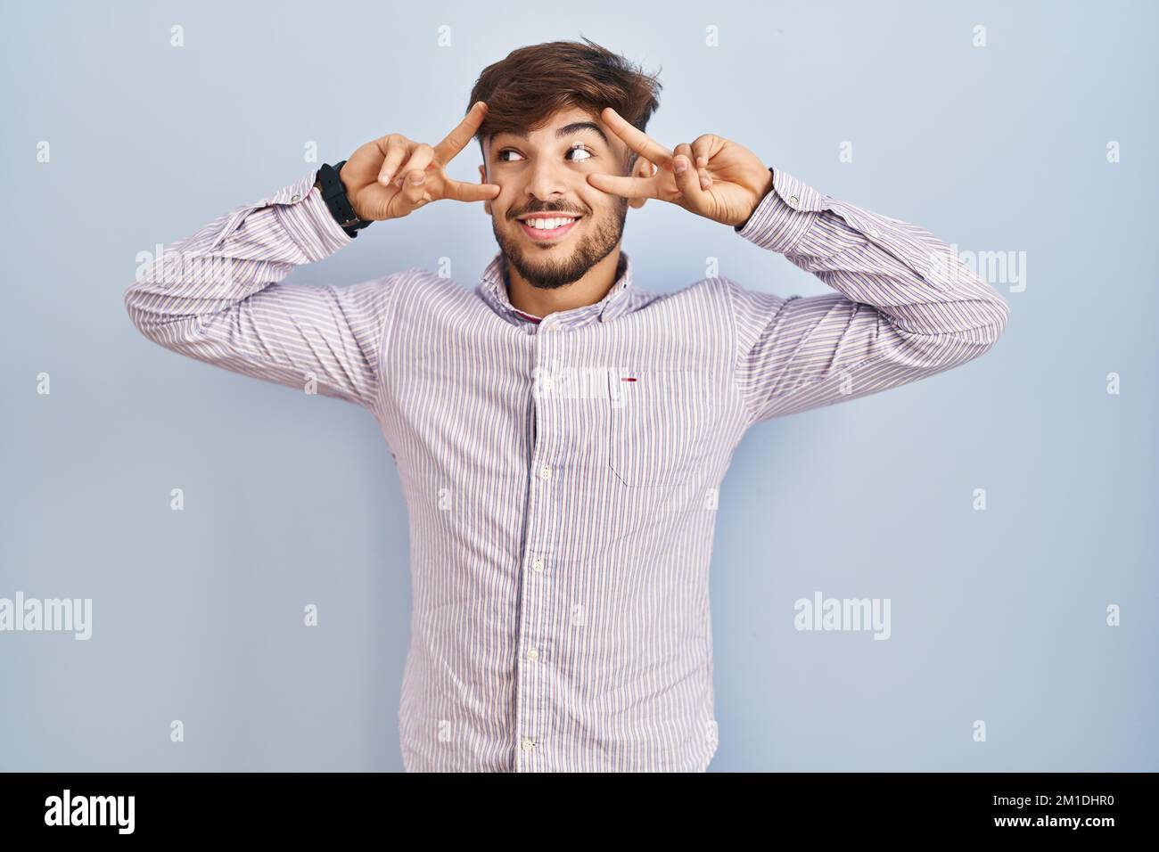 Arab man with beard standing over blue background doing peace symbol ...