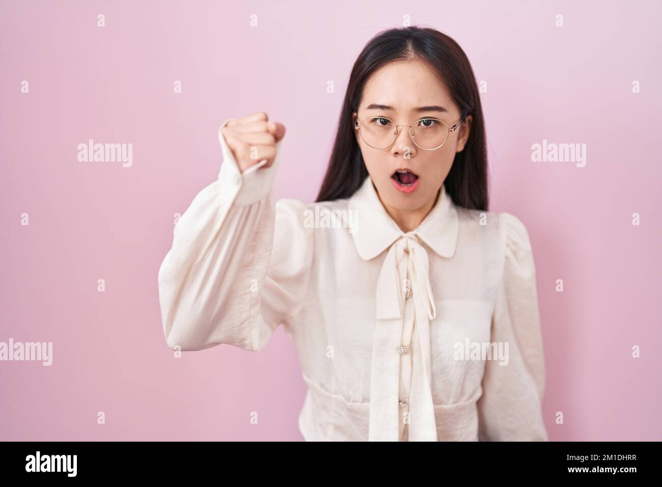 Young chinese woman standing over pink background angry and mad raising ...