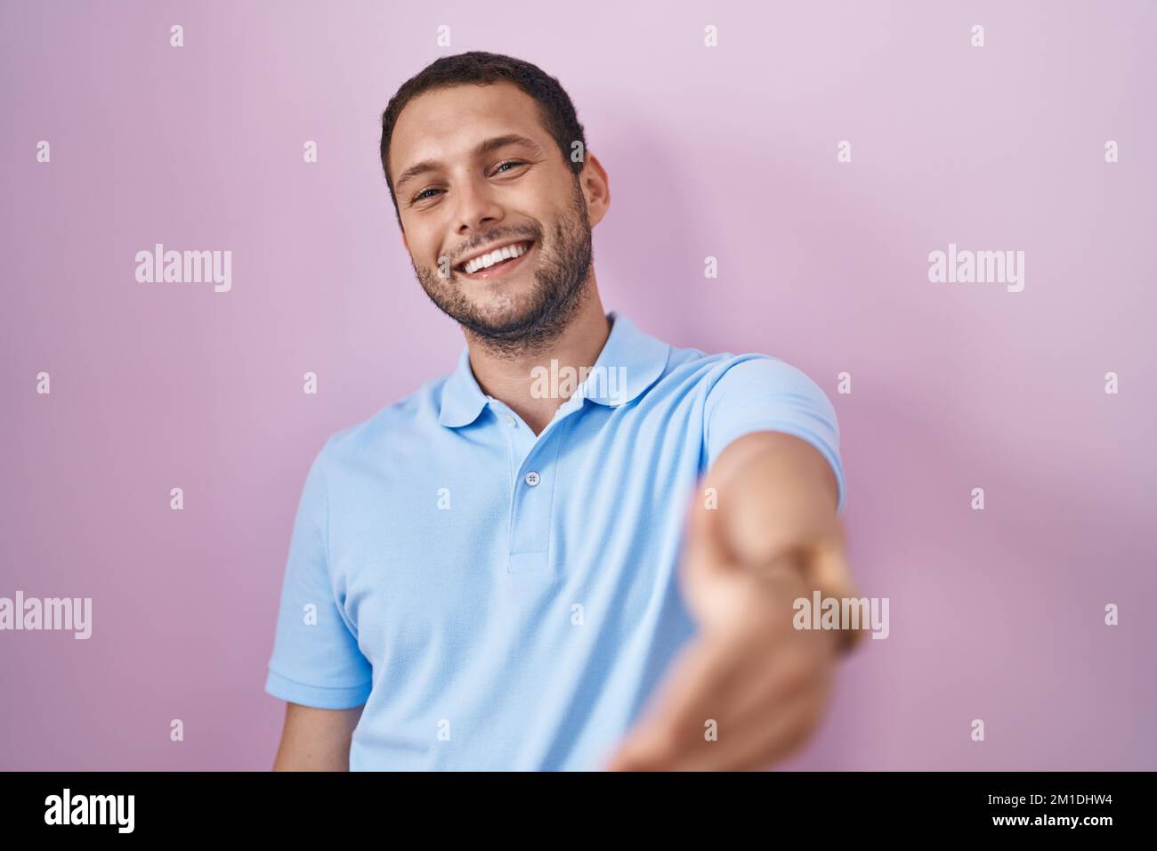 Hispanic man standing over pink background smiling friendly offering ...