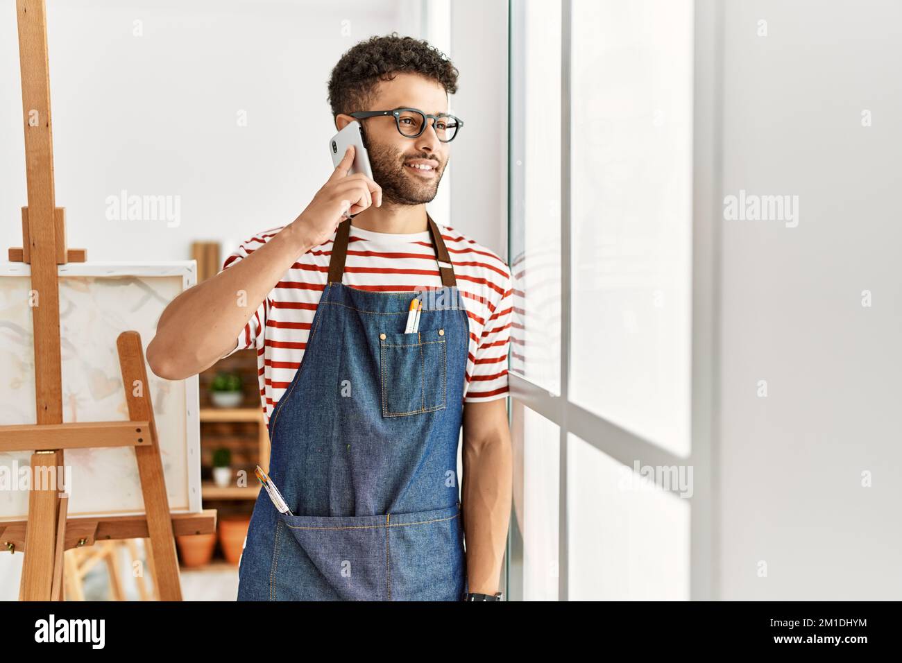 Young arab artist man smiling happy using smartphone at art studio ...