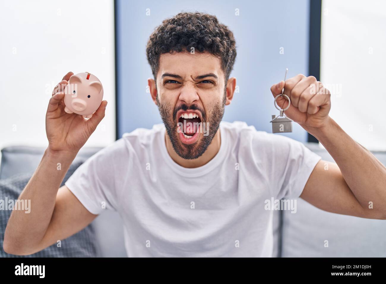Arab man holding piggy bank and house keys angry and mad screaming ...