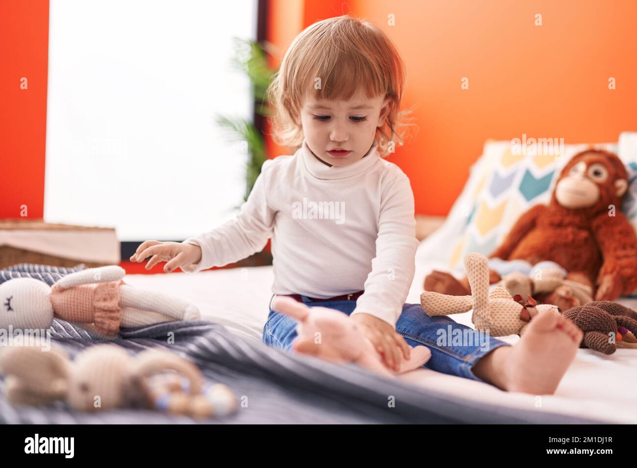Adorable hispanic girl holding dolls sitting on bed at bedroom Stock ...