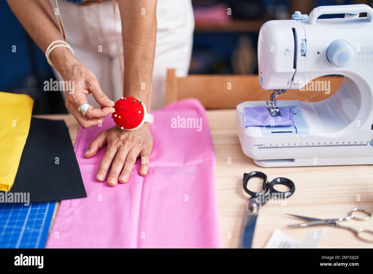 Middle age grey-haired woman tailor cutting cloth at sewing studio ...