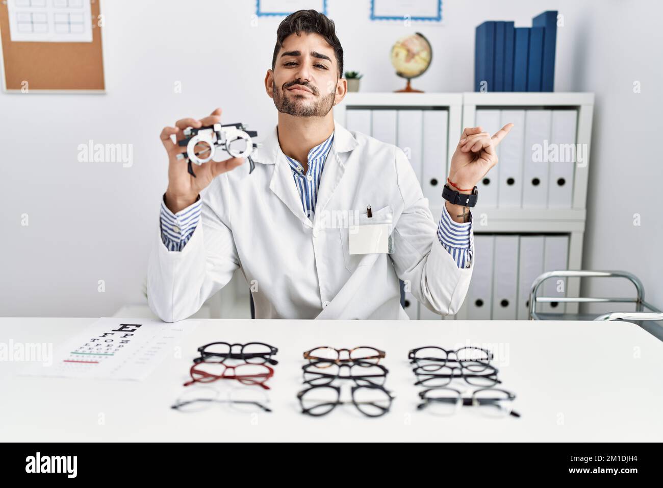 Young optician man holding optometry glasses pointing with hand finger ...