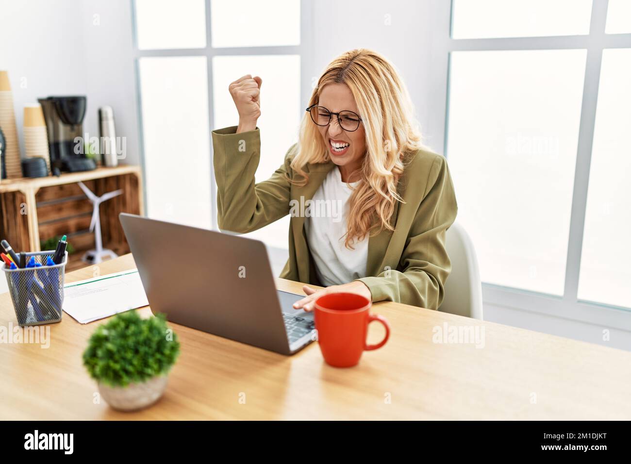Beautiful blonde woman working at the office with laptop angry and mad ...