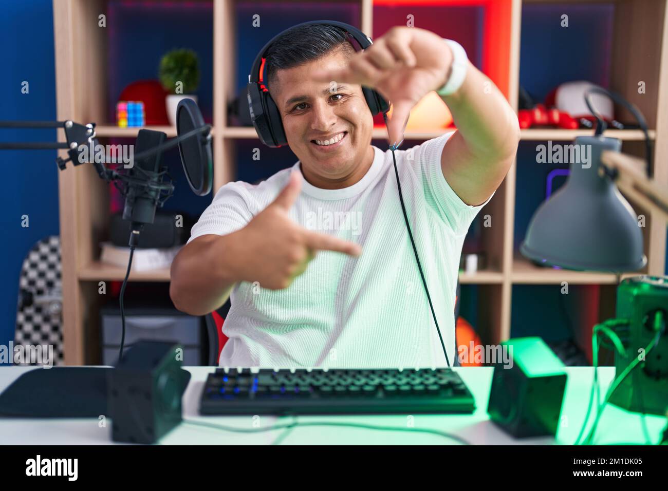 Young hispanic man playing video games smiling making frame with hands ...