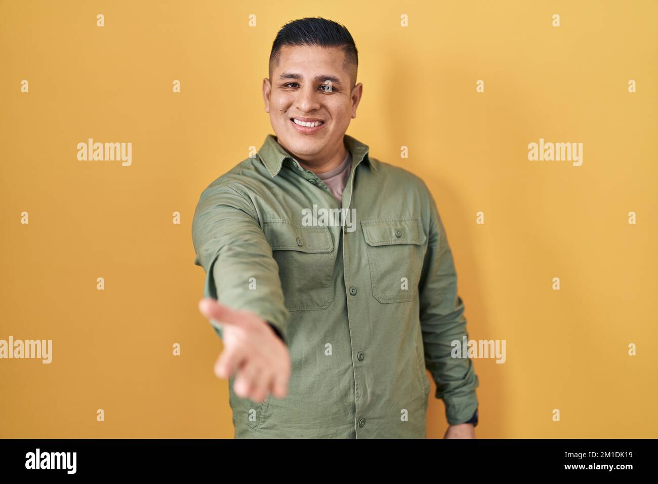Hispanic young man standing over yellow background smiling cheerful ...