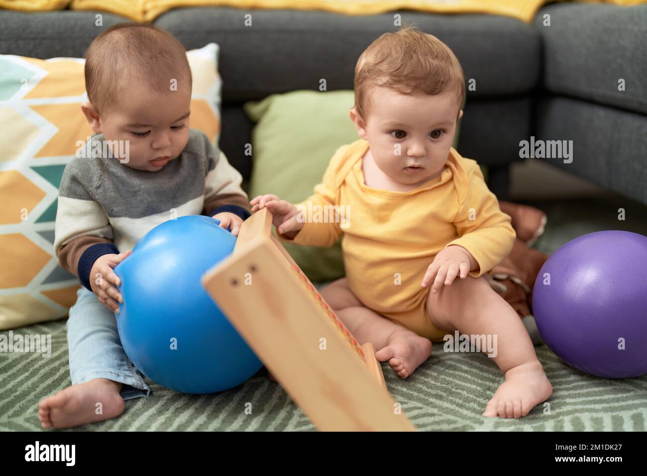 Two toddlers playing with balls sitting on floor at home Stock Photo ...