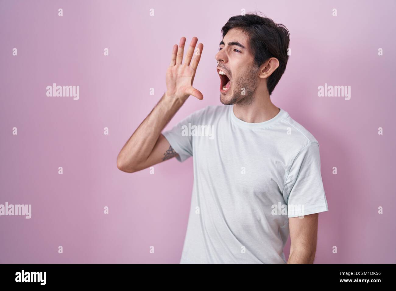 Young hispanic man standing over pink background shouting and screaming ...
