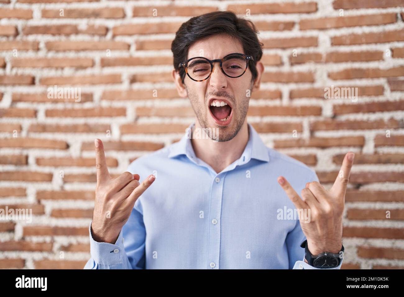 Young hispanic man standing over brick wall background shouting with ...