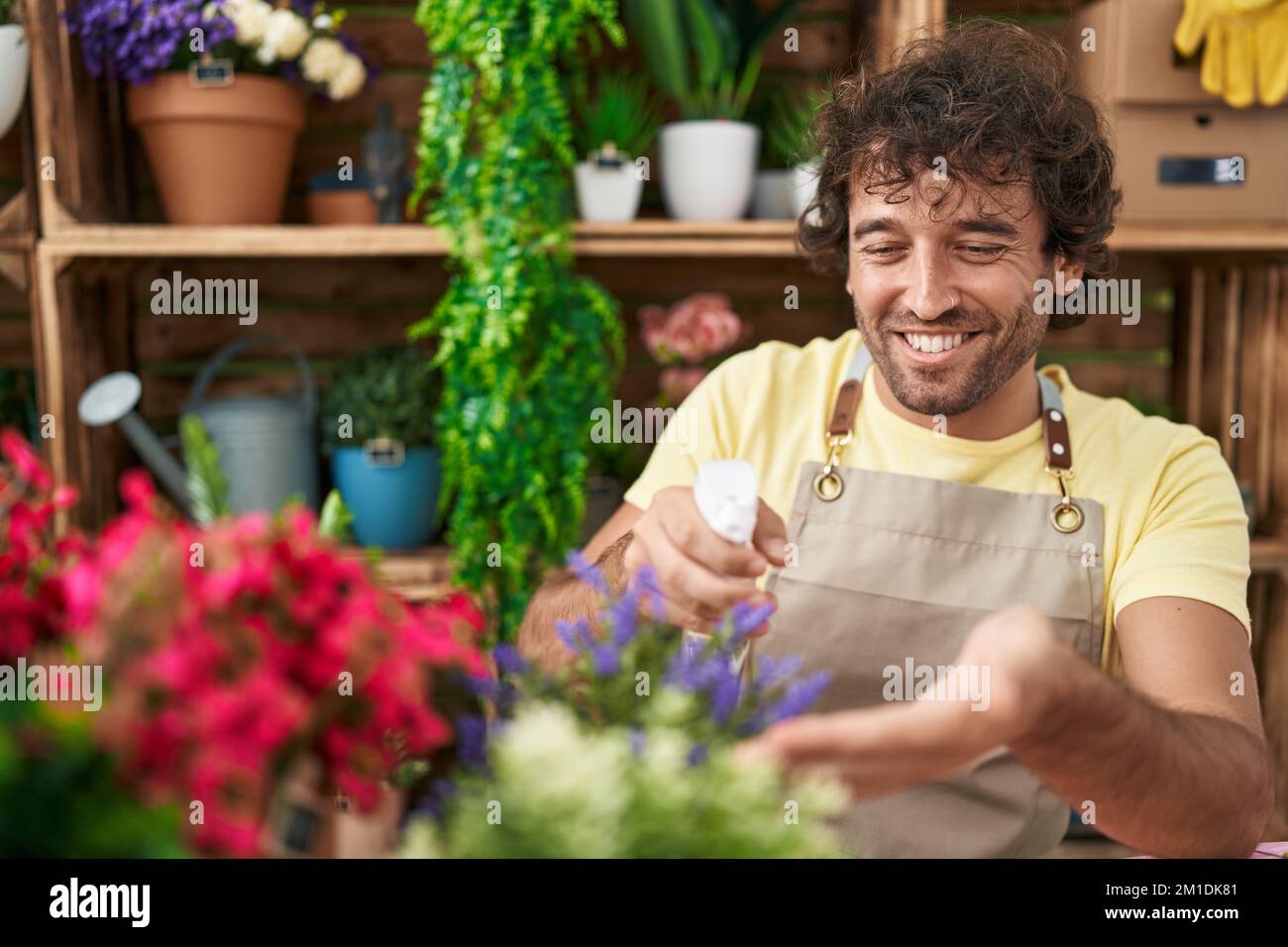 Young hispanic man florist using diffuser watering plant at flower shop ...