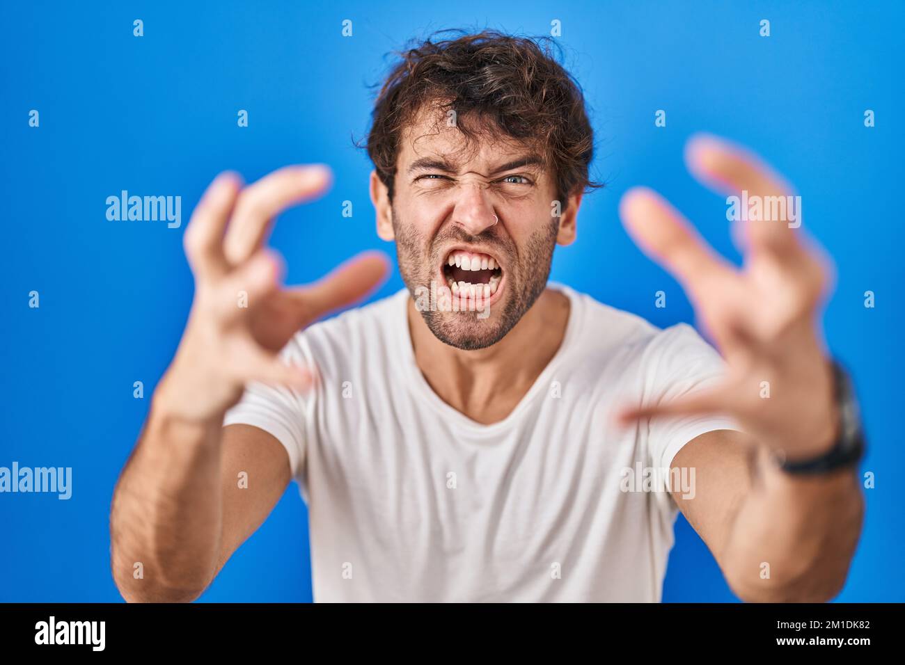 Hispanic young man standing over blue background shouting frustrated ...