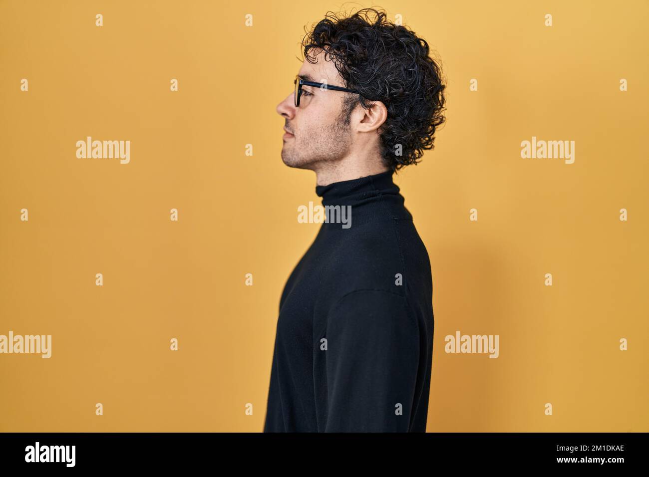 Hispanic man standing over yellow background looking to side, relax ...