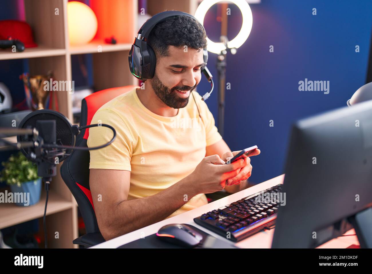 Young arab man streamer using computer and smartphone at gaming room ...