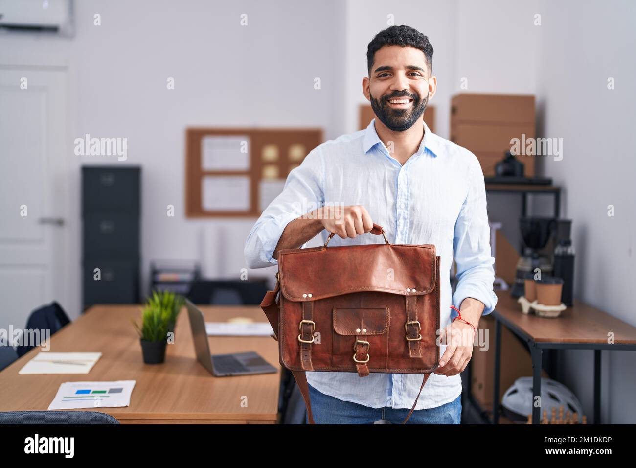 Hispanic man with beard working at the office holding briefcase looking ...