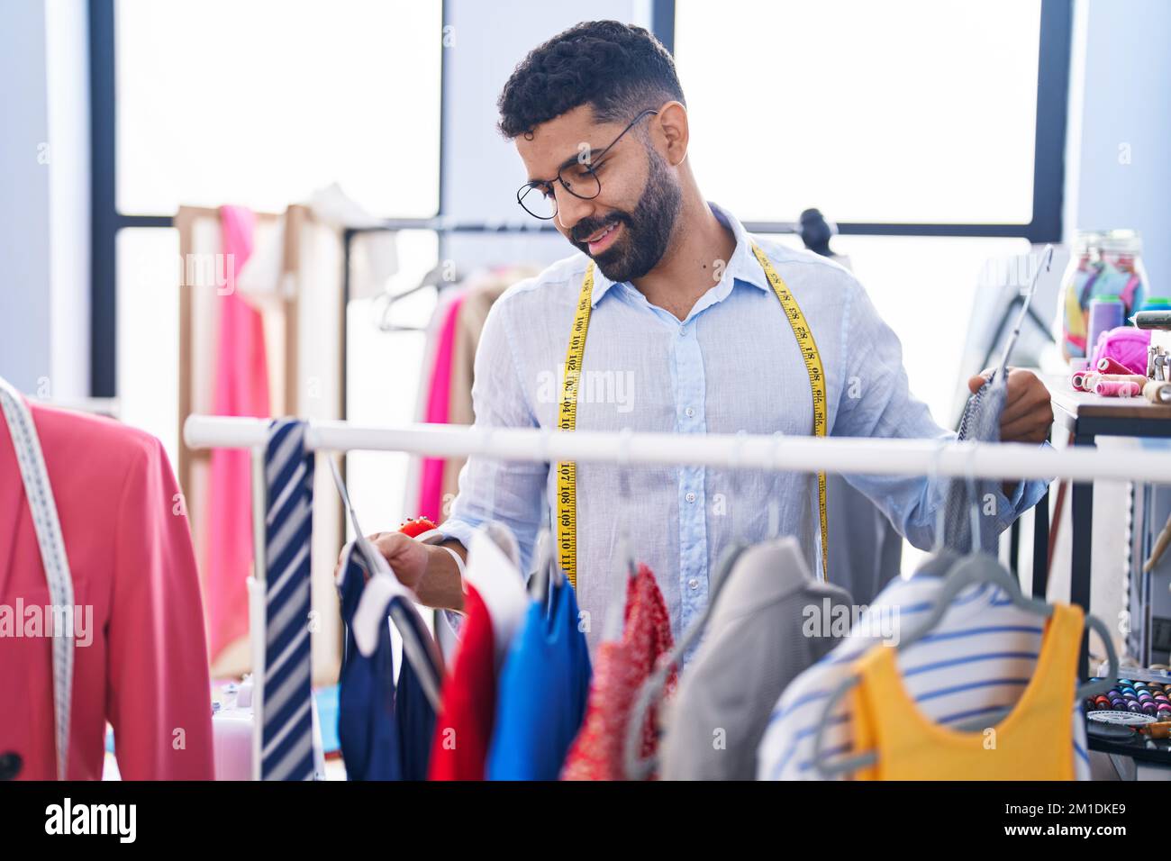 Young arab man tailor smiling confident holding clothes on rack at ...