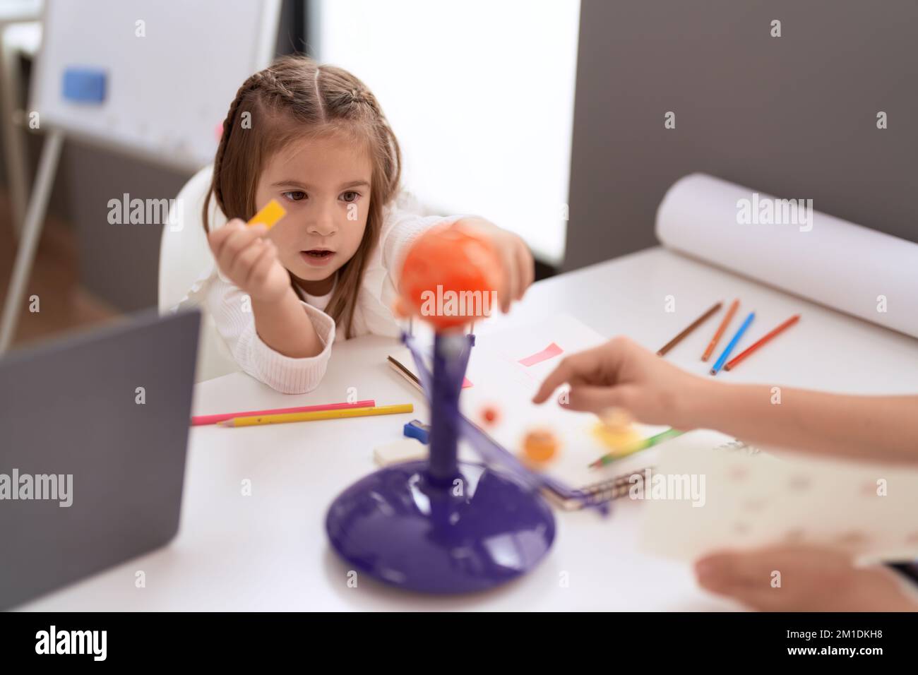 Adorable hispanic girl learning universe sitting on table at classroom ...