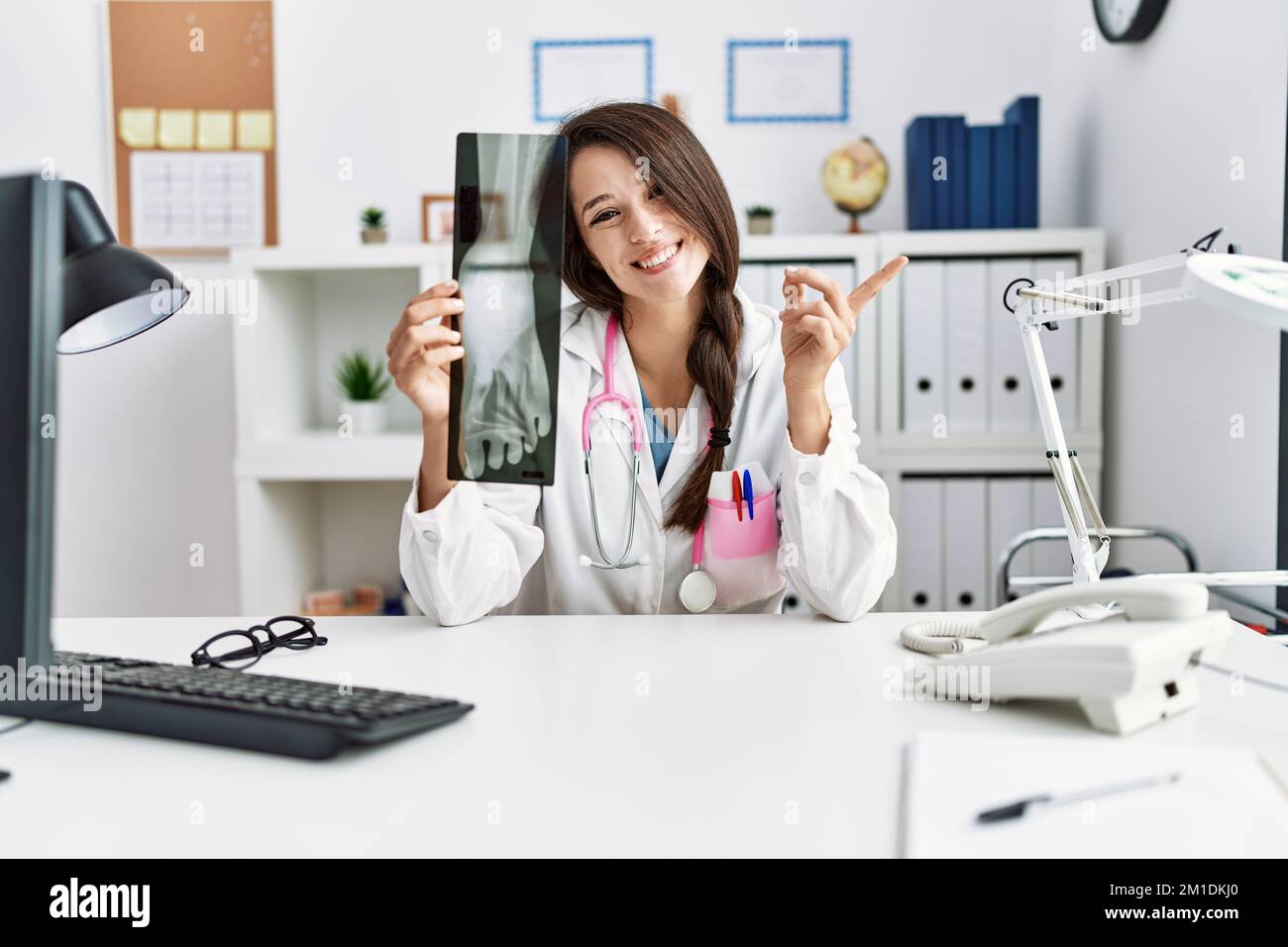 Young doctor woman holding foot x-ray smiling happy pointing with hand ...