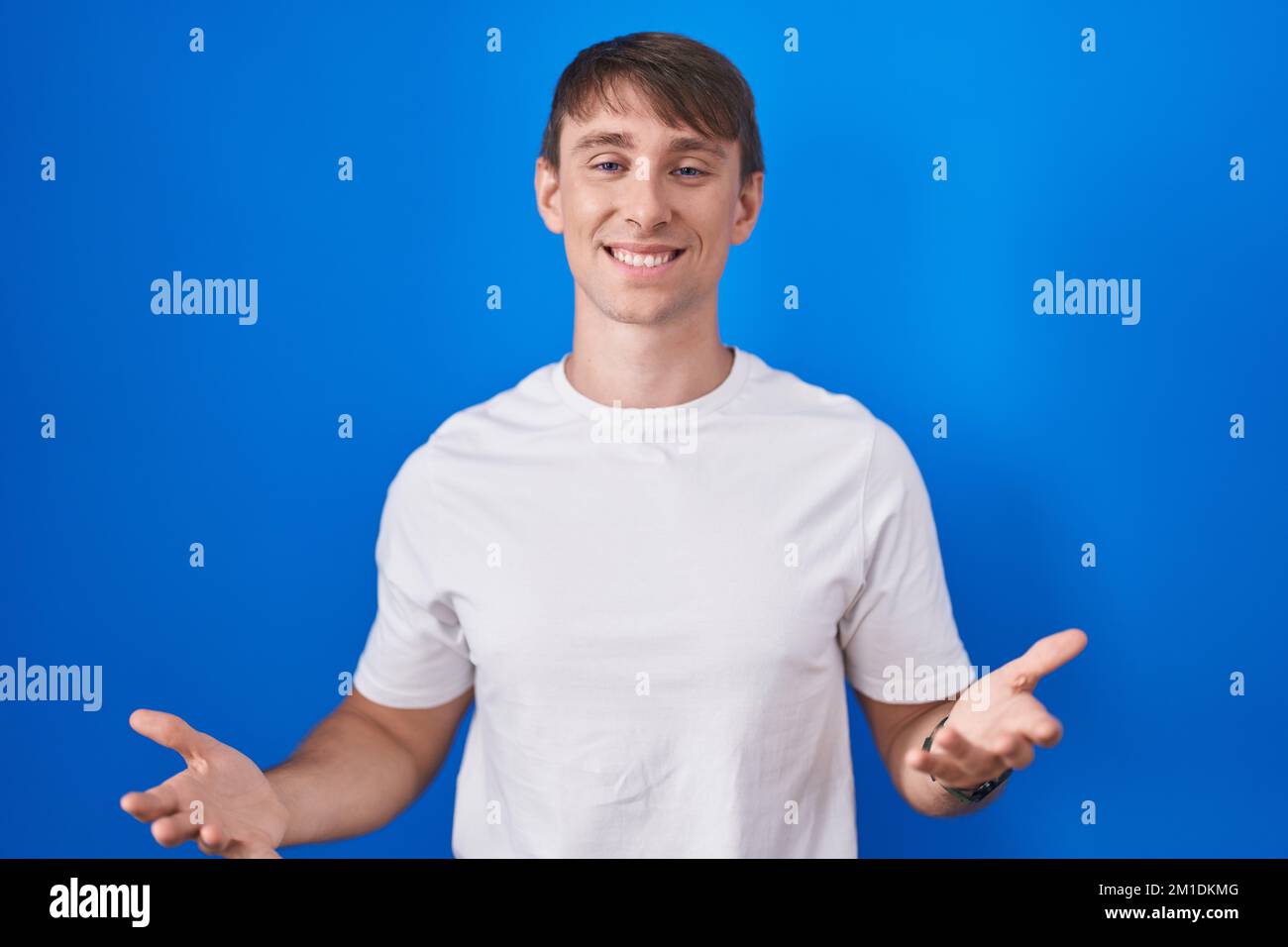 Caucasian blond man standing over blue background smiling cheerful with ...
